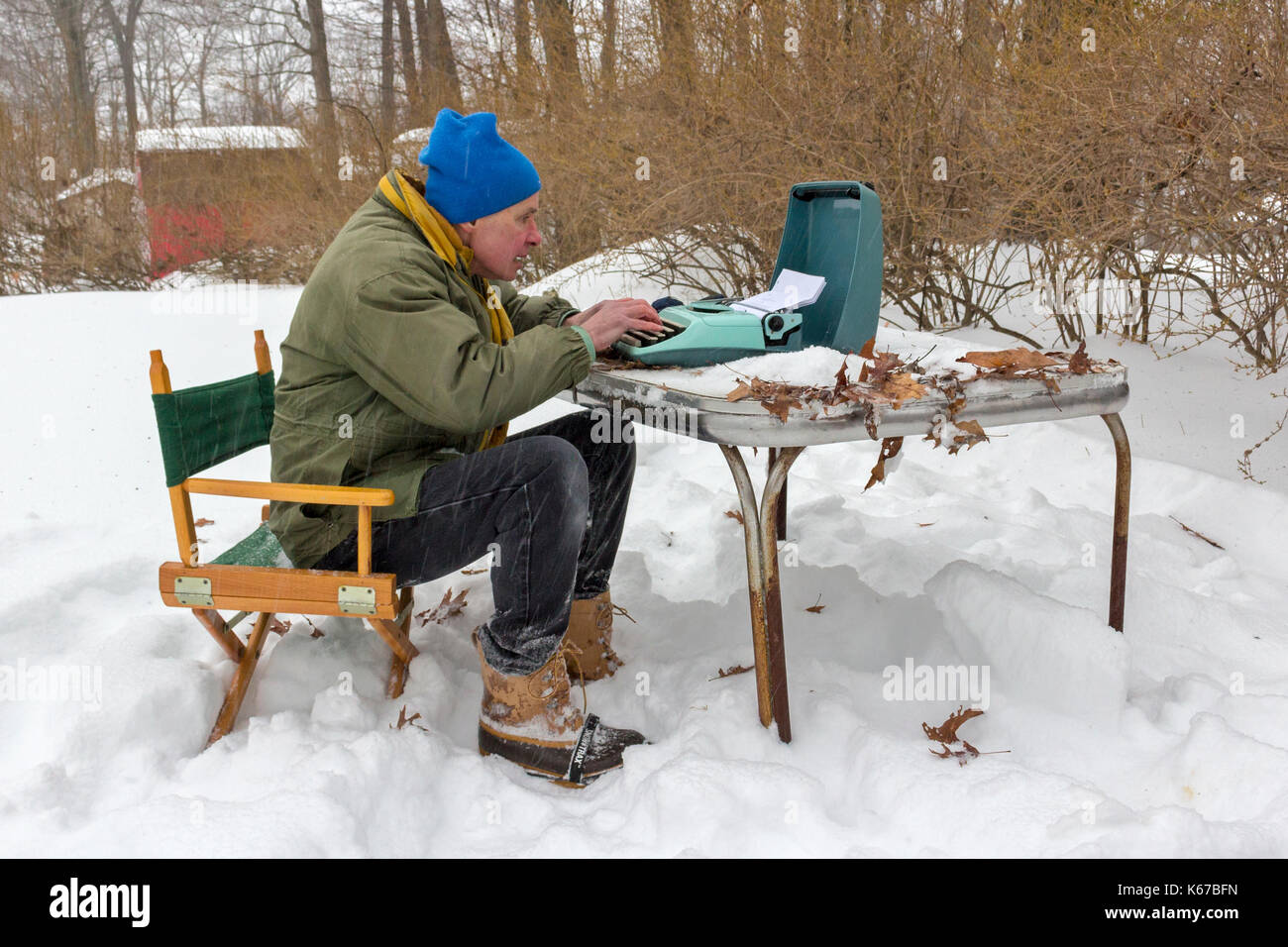 A writer sitting at a table outside during a snowstorm and typing on a ...