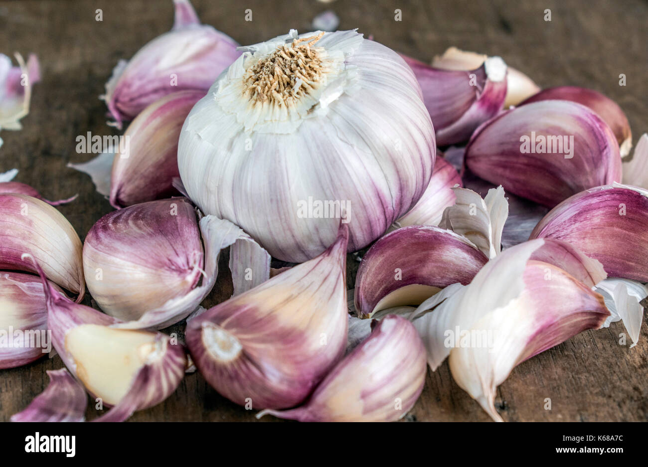 Whole purple garlic bulb and many garlic cloves on top of a wooden ...
