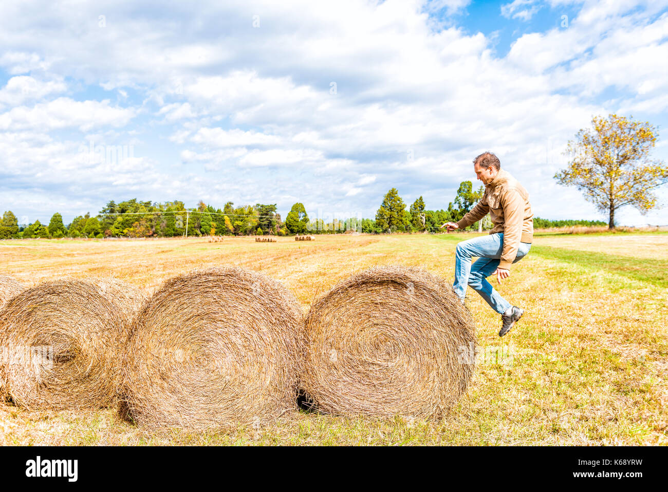 Young man jumping in air over hay roll bales in a farm rural ...