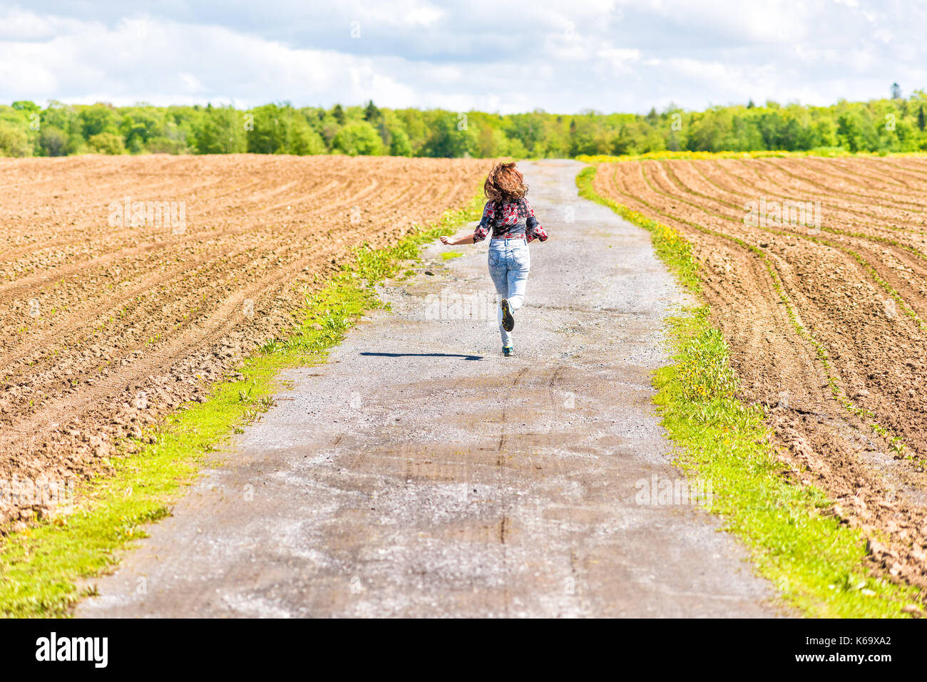 Back of young woman running, jumping in air and smiling on dirt ...