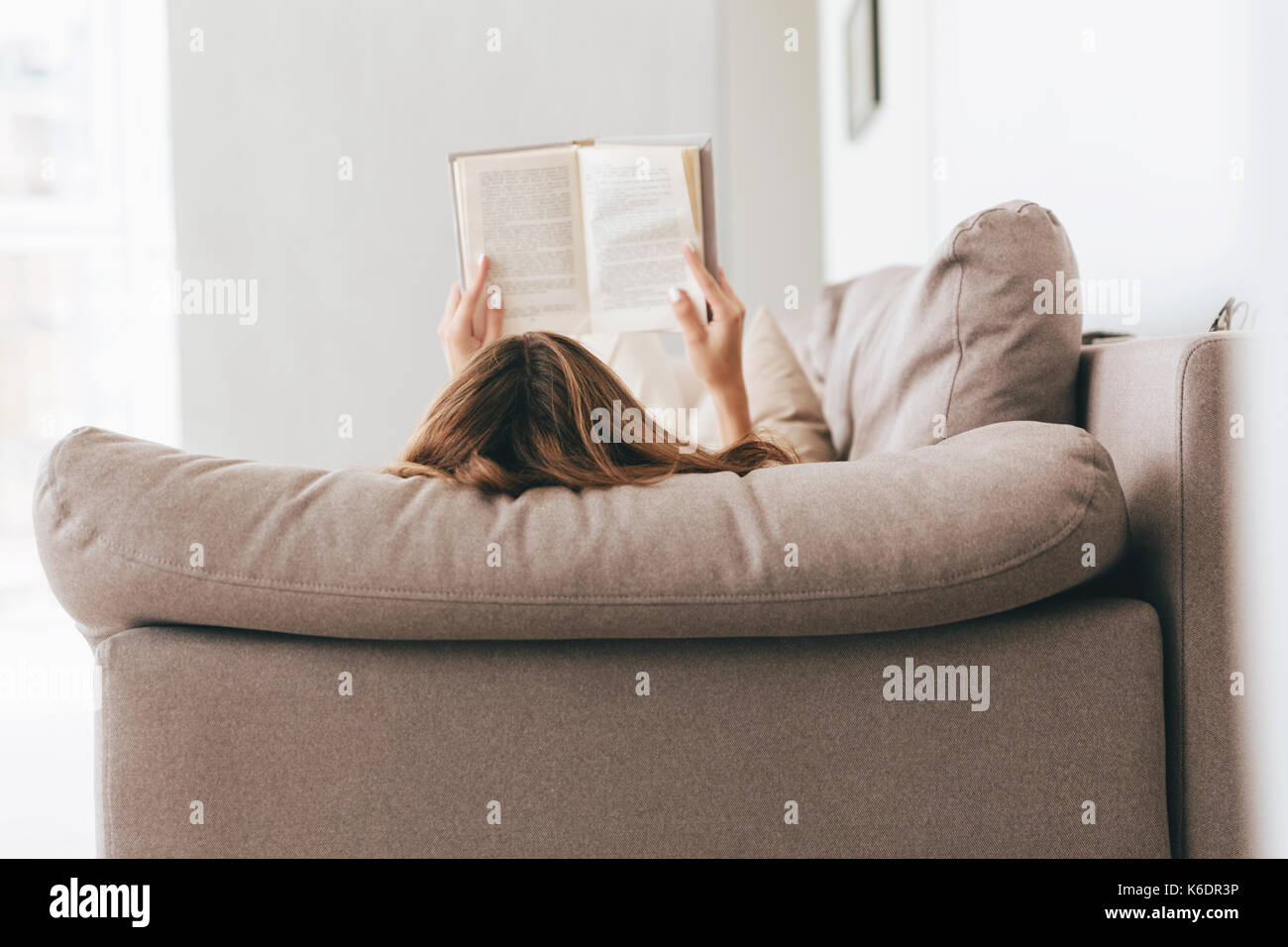 Back view of woman lying on sofa and reading book at home Stock Photo ...
