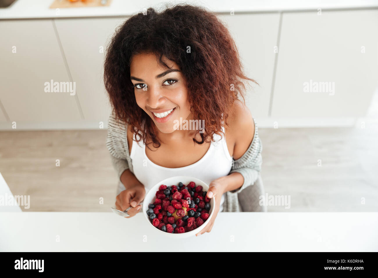 Young happy african woman eating breakfast and fruits in kitchen in the ...