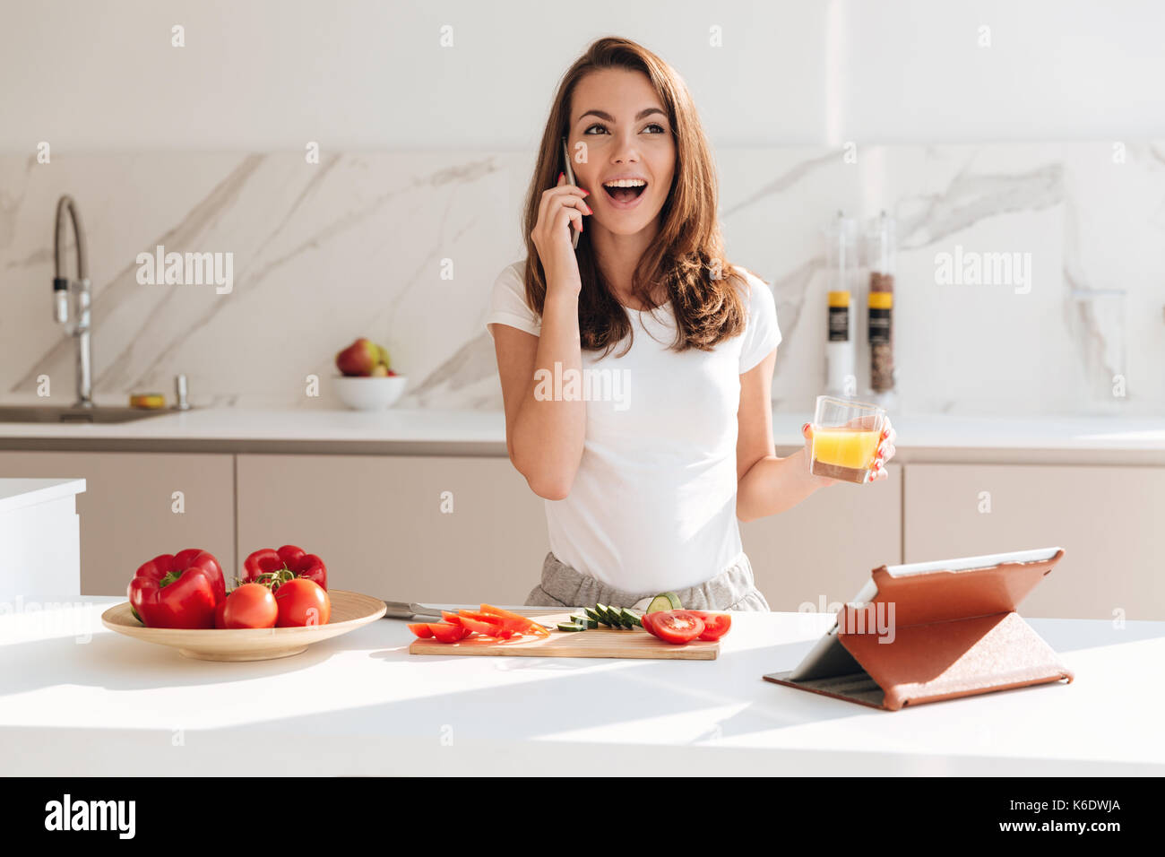 Happy excited woman talking on mobile phone while cooking in a kitchen ...