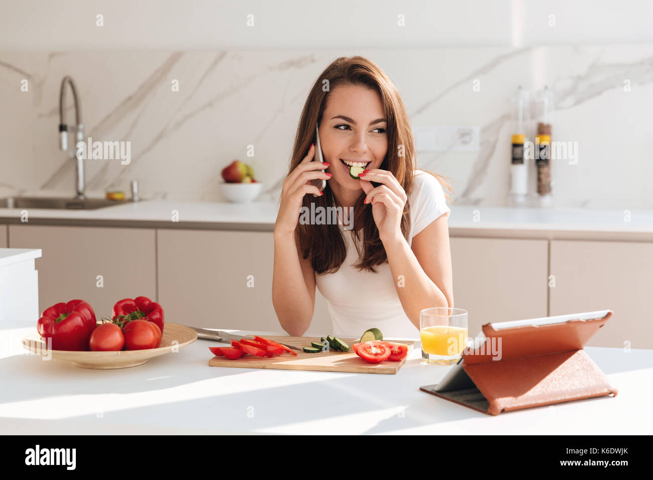 Happy smiling woman talking on mobile phone while cooking in a kitchen ...