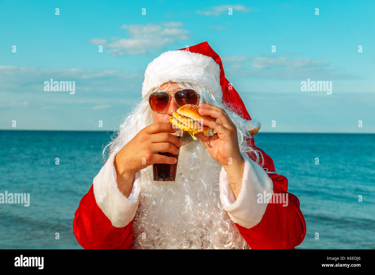 Santa Claus on the beach eating a hamburger. The concept of unhealthy ...