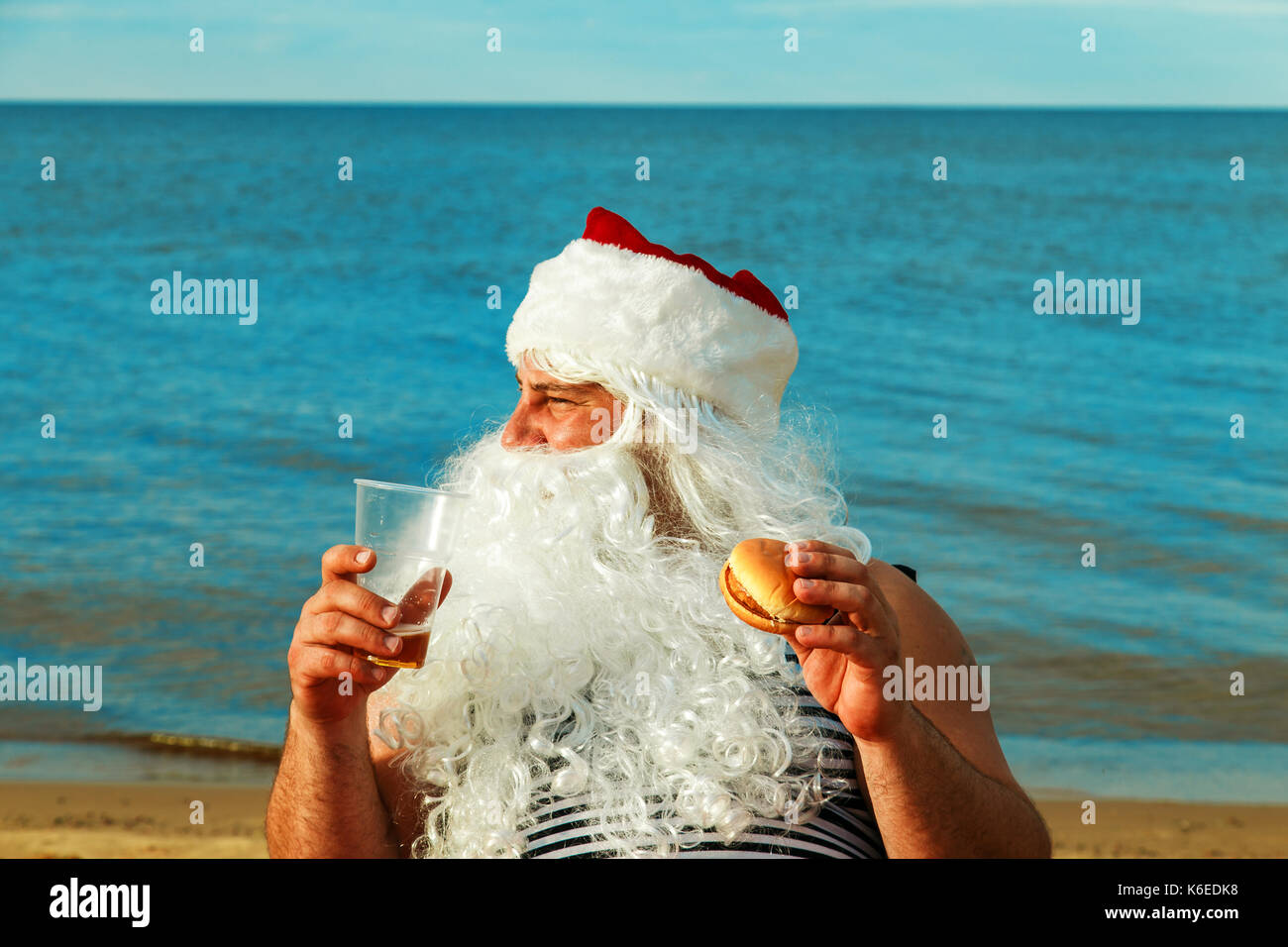 Santa Claus on the beach eating a hamburger. The concept of unhealthy ...