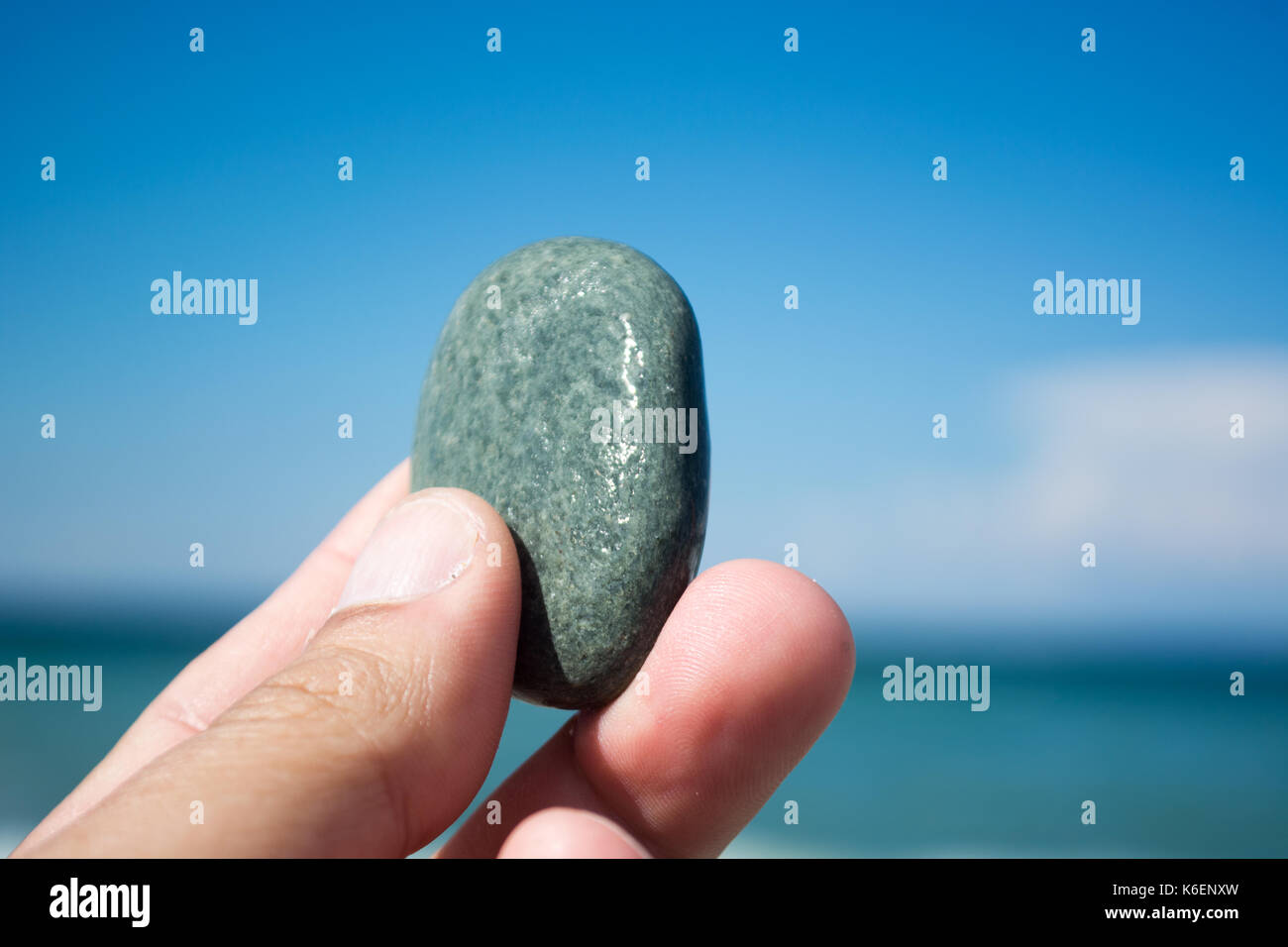 Hand with small stone with sea as background Stock Photo - Alamy