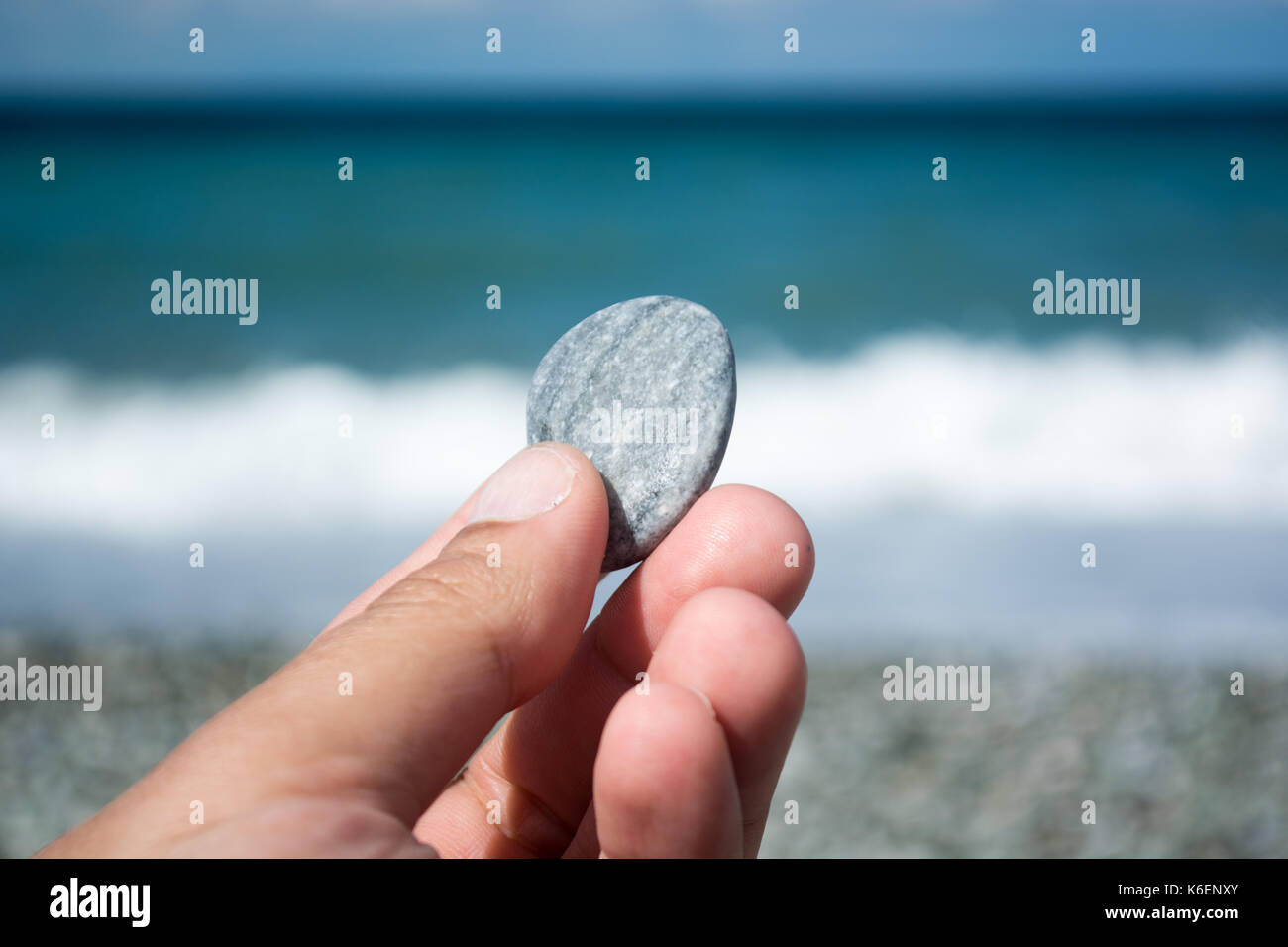 Hand with small stone with sea as background Stock Photo - Alamy