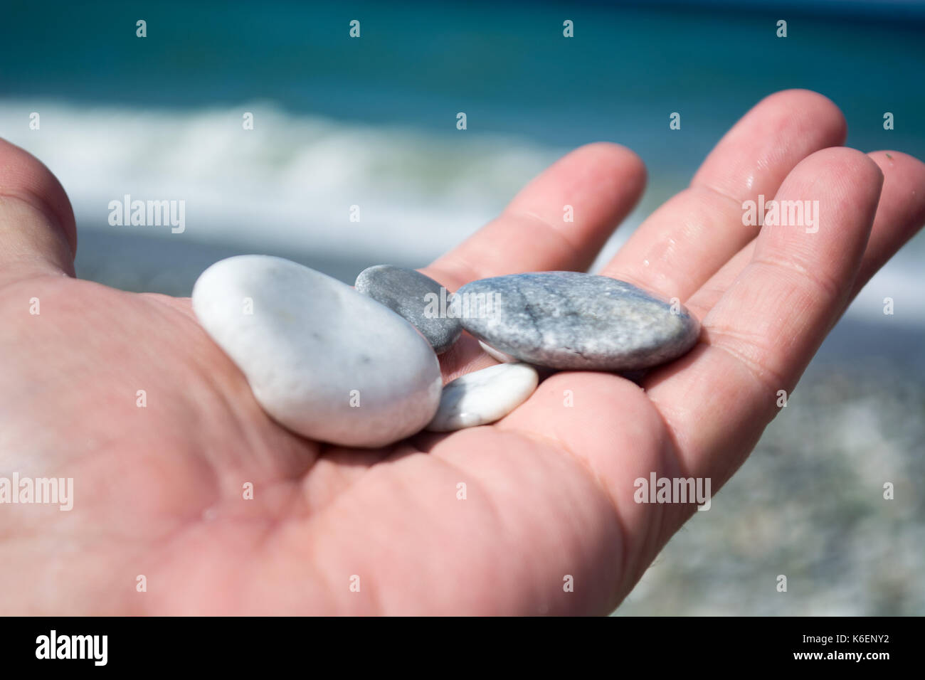 Hand full with small stones with sea as background Stock Photo - Alamy