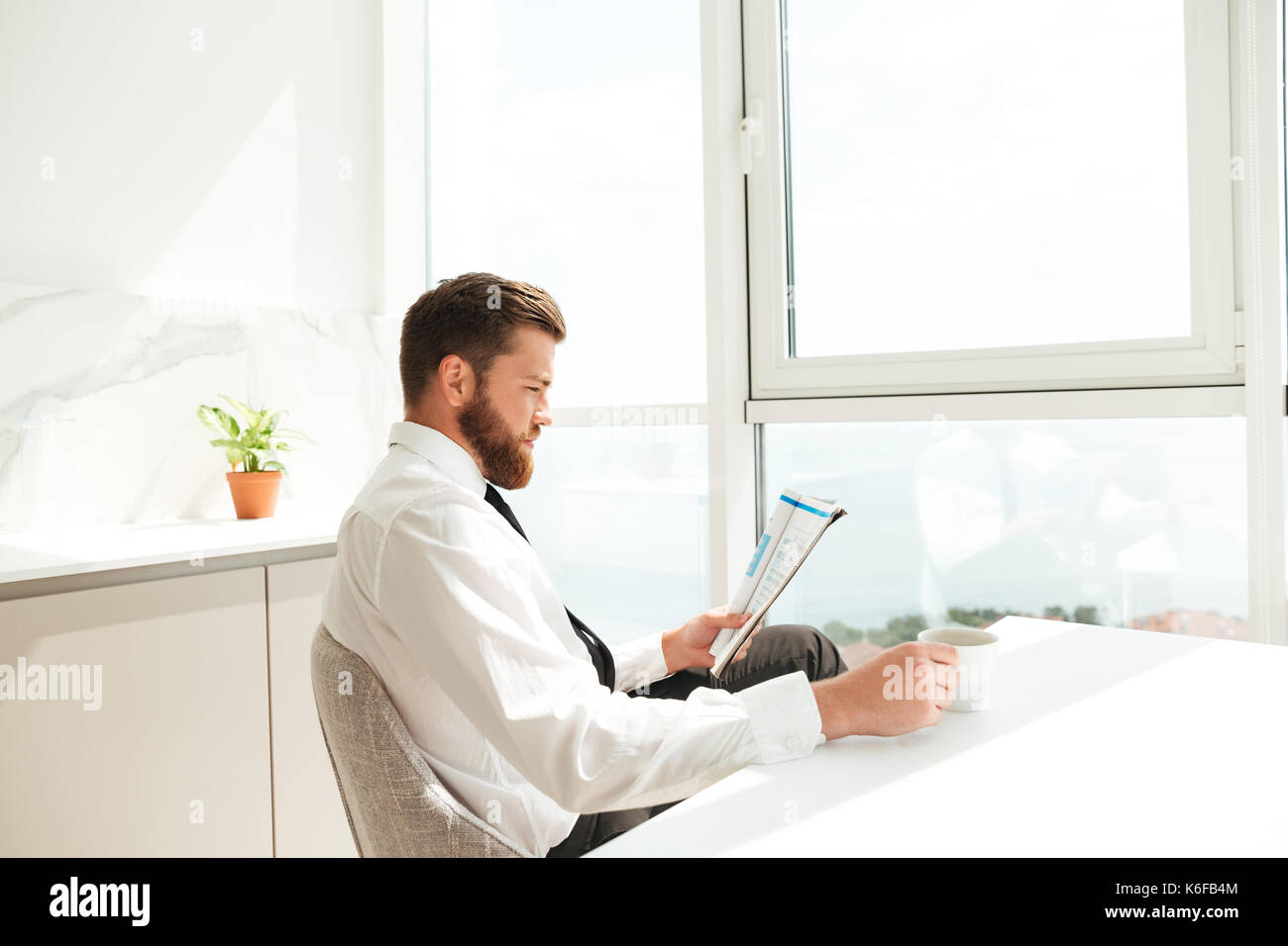 Side view of bearded man in business clothes sitting by the table on ...