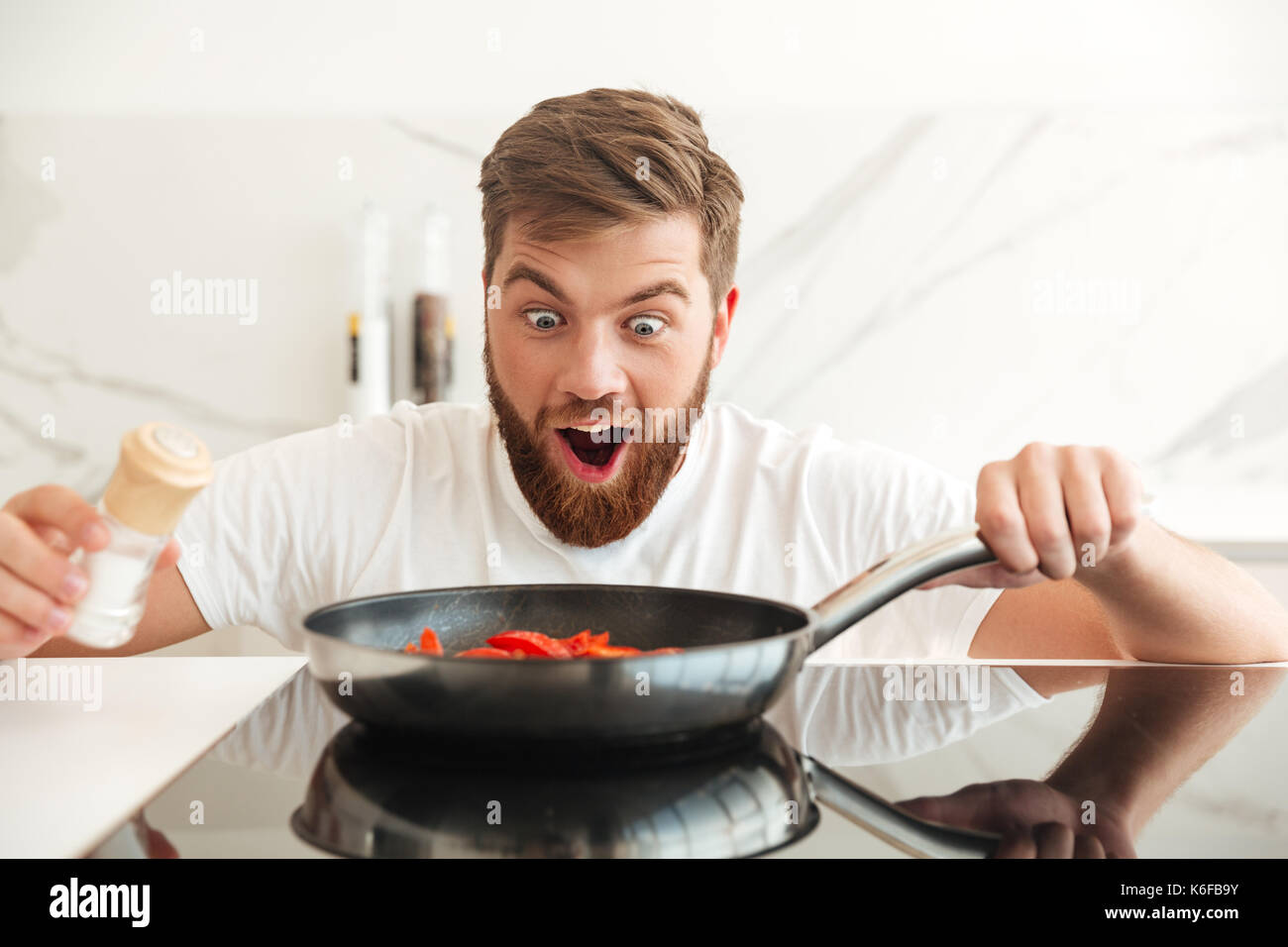 Happy shocked bearded man sprinkle with salt of vegetables in kitchen ...