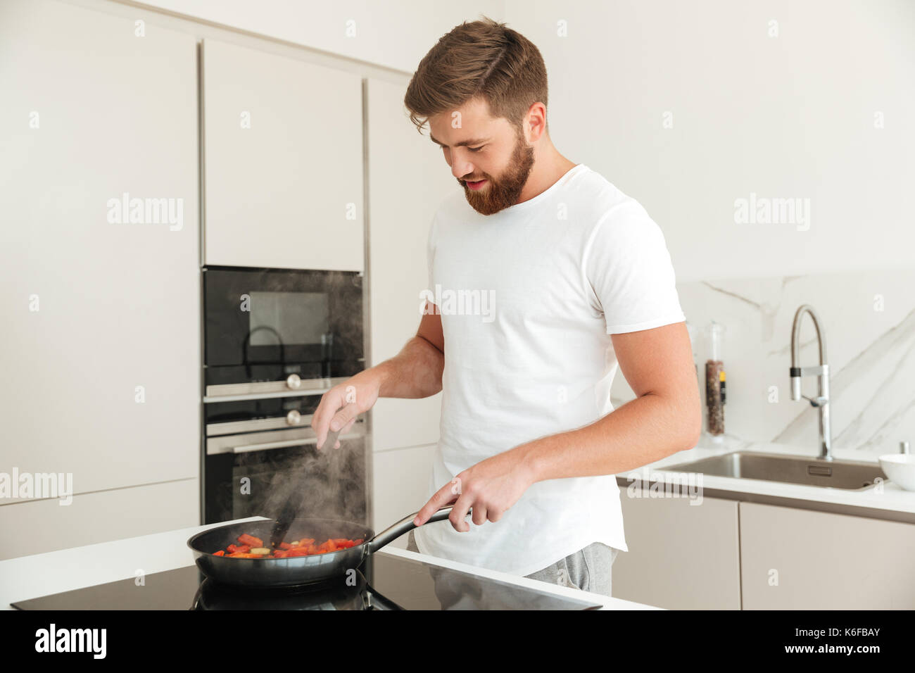Side view of pleased bearded man cooking on kitchen Stock Photo - Alamy