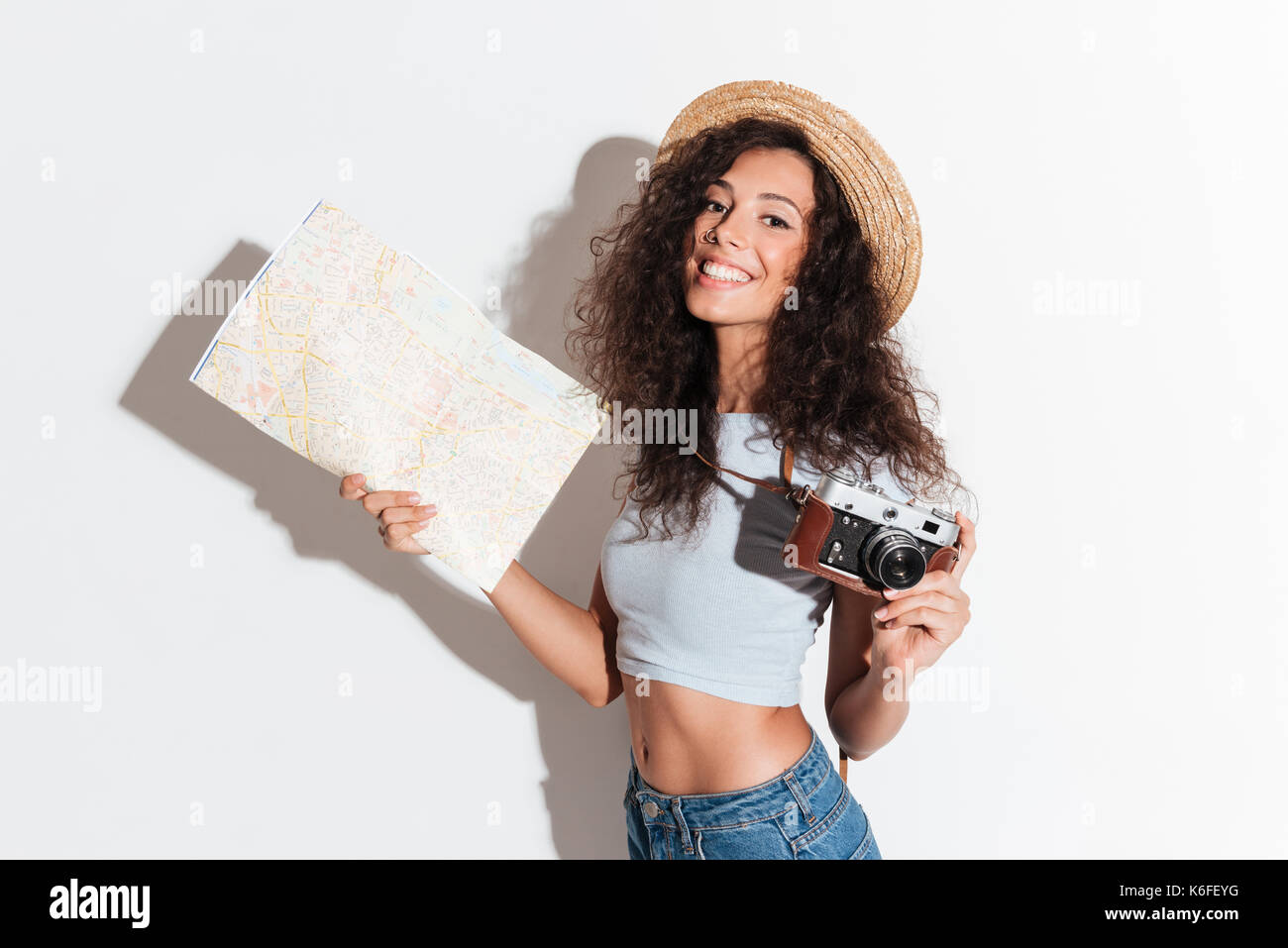 Pretty woman with curly hair and in hat holding map and retro camera ...