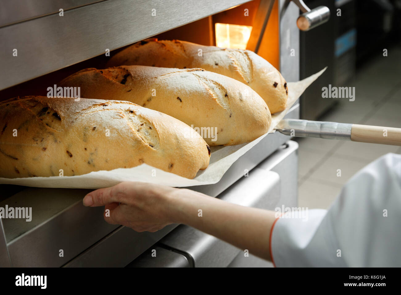 Hands of a baker getting hot bread loafs ot of the oven on a small ...