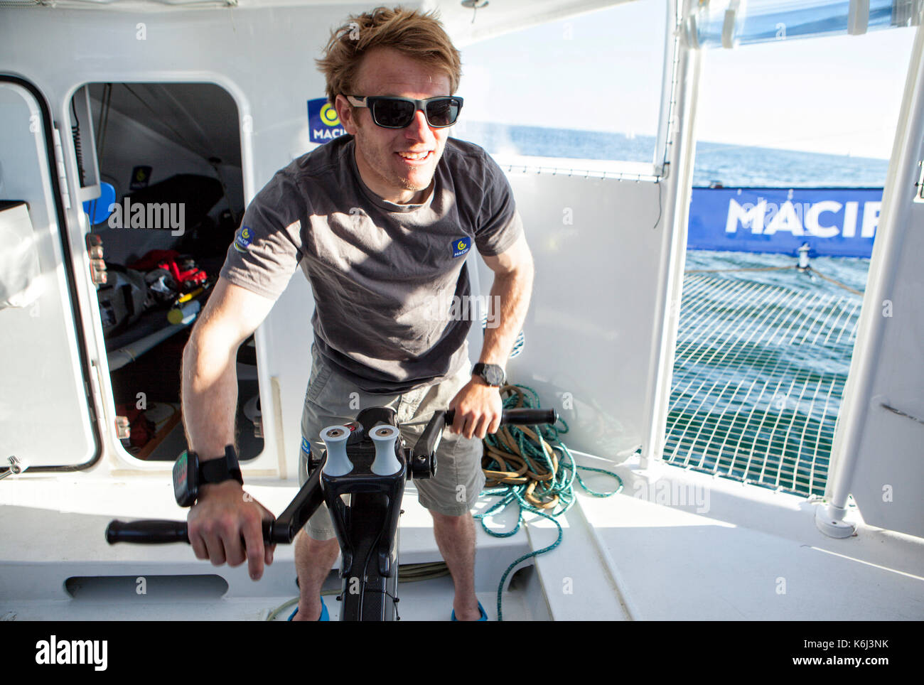 Sailor maneuvering on winch inside cockpit of trimaran, Atlantic Ocean ...