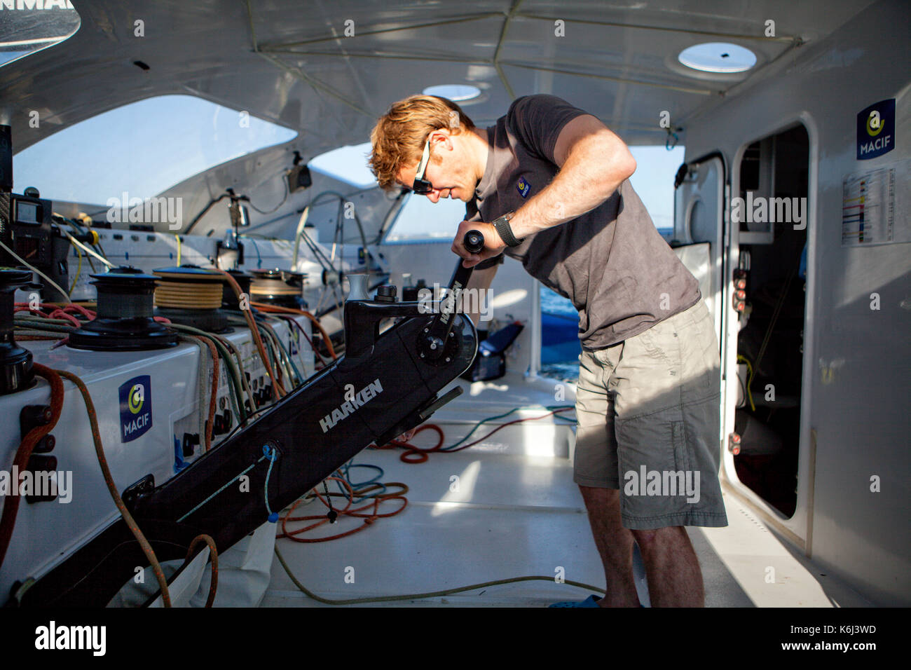 Sailor maneuvering on winch inside cockpit of trimaran, Atlantic Ocean ...