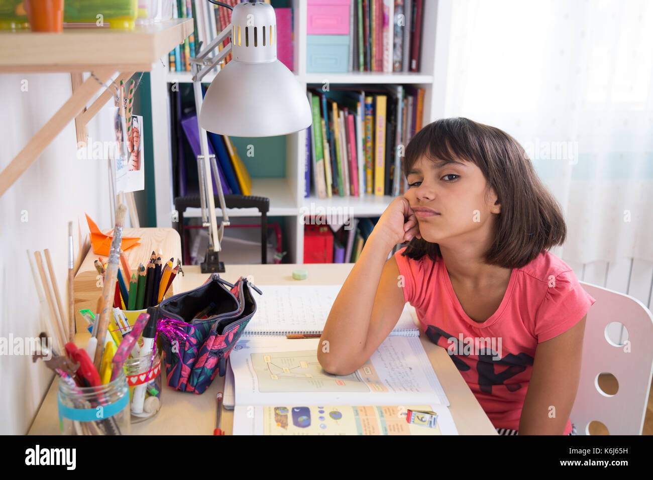 Bored school girl doing homework at home. Looking at camera Stock Photo ...