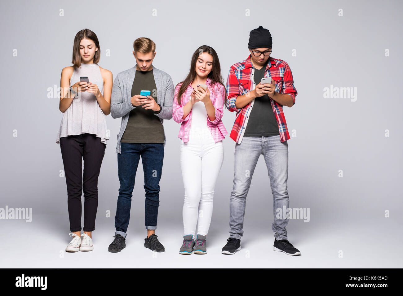 Diverse students standing and using modern gadgets isolated over grey ...