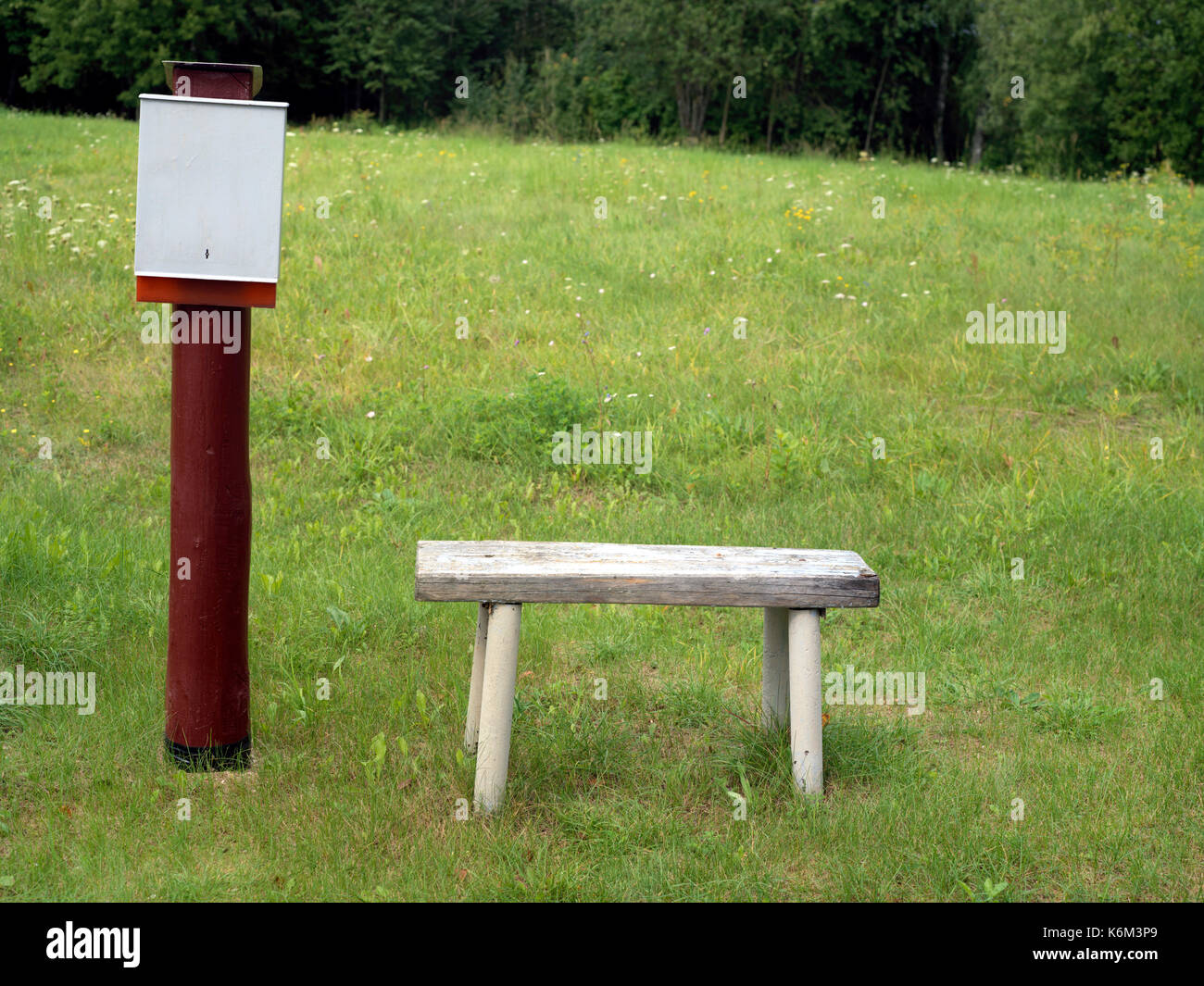 Post box and wooden bench in the open field, a forest in the background ...