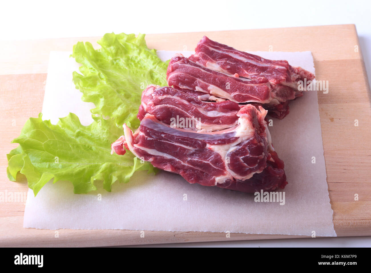 Raw beef edges and lettuce leaf on wooden desk isolated on white ...