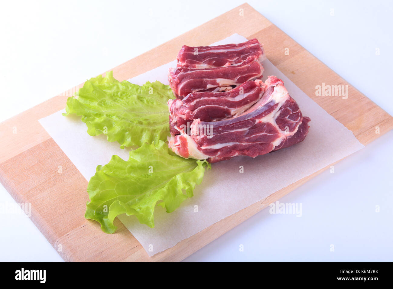 Raw beef edges and lettuce leaf on wooden desk isolated on white ...