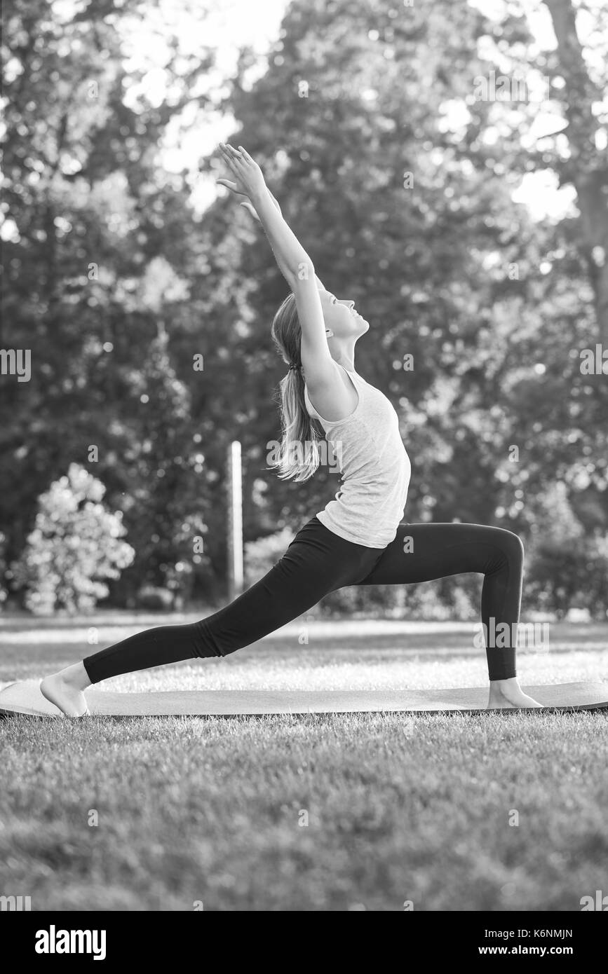 Monochrome vertical shot of a young fitness woman practicing yoga at ...