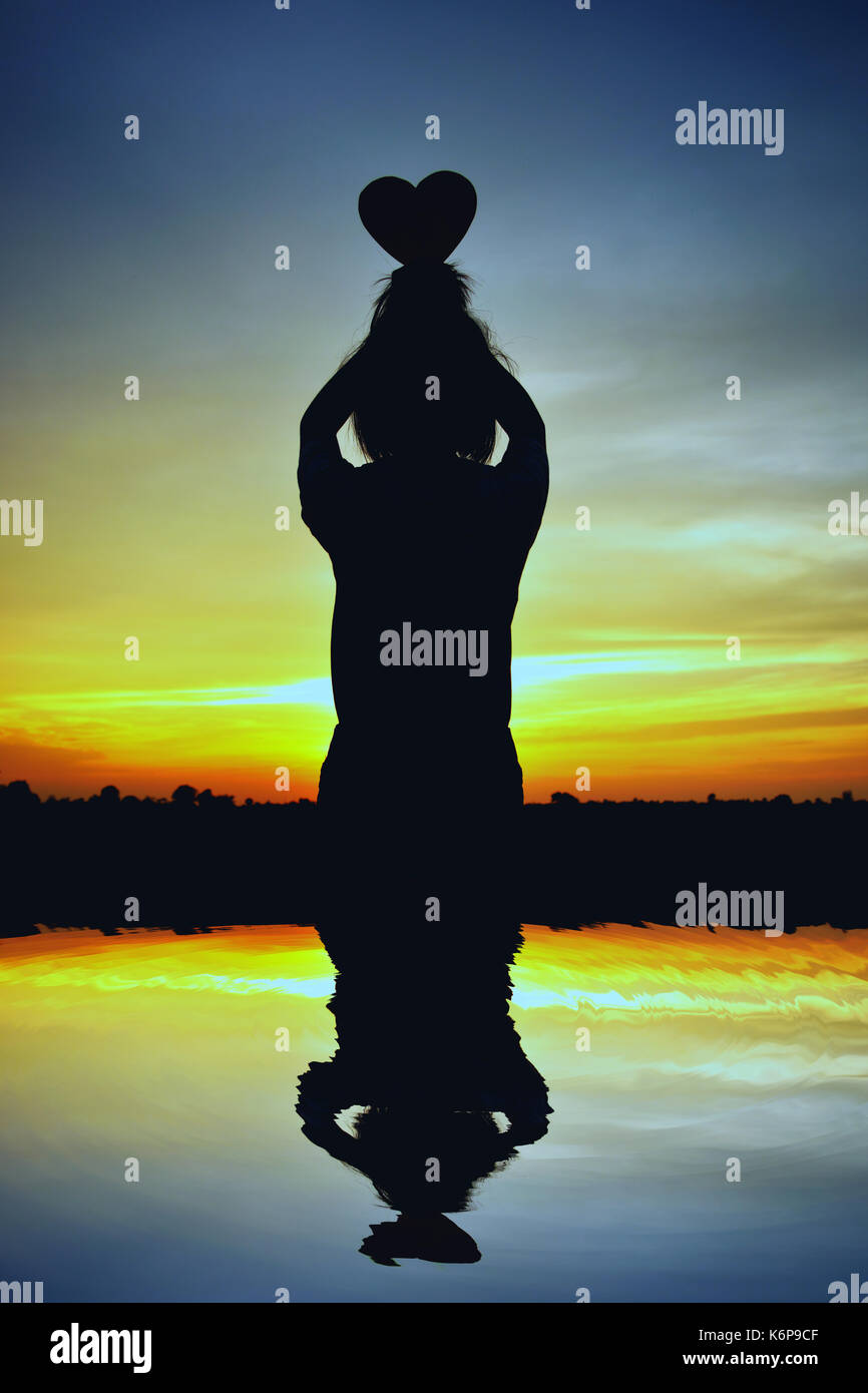 Silhouette of a girl holding heart shape on head turn face to the sun ...