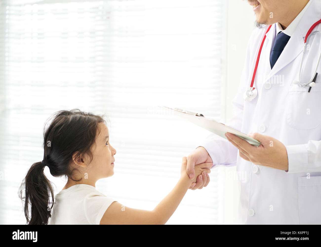 Unknown smile and friendly doctor and happy little girl shaking hands ...