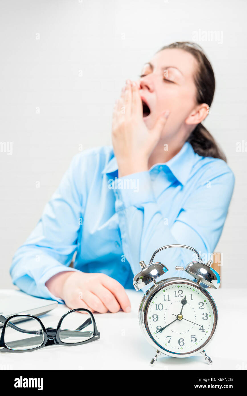 Tired yawning woman in an office out of focus and an alarm clock ...