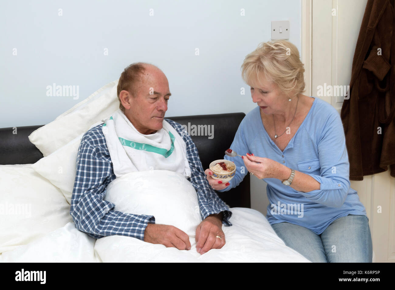 An elderly sick bedridden man being fed breakfast by his wife and carer ...