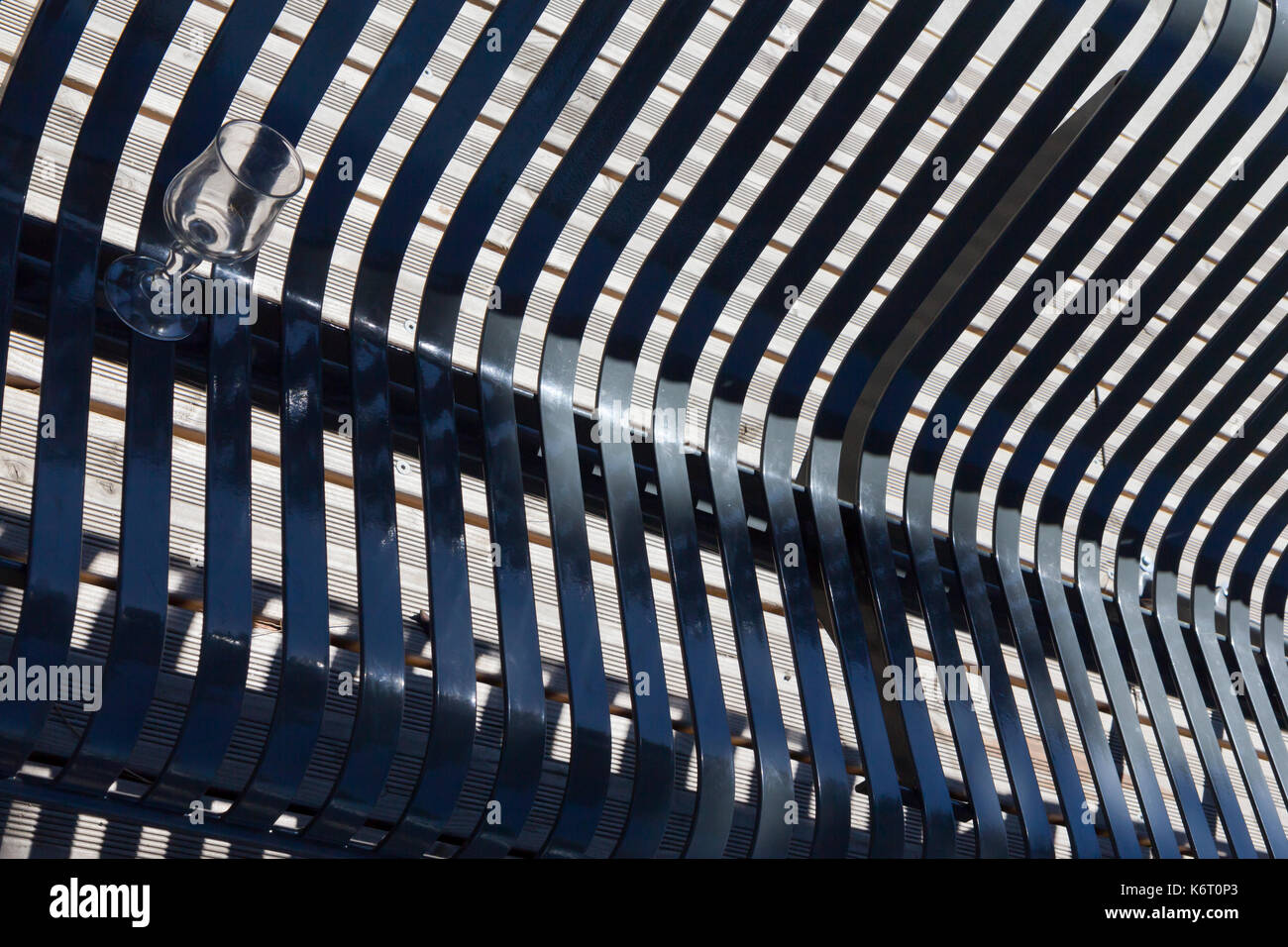 Steel slatted bench at a jaunty angle with a wine glass Stock Photo - Alamy