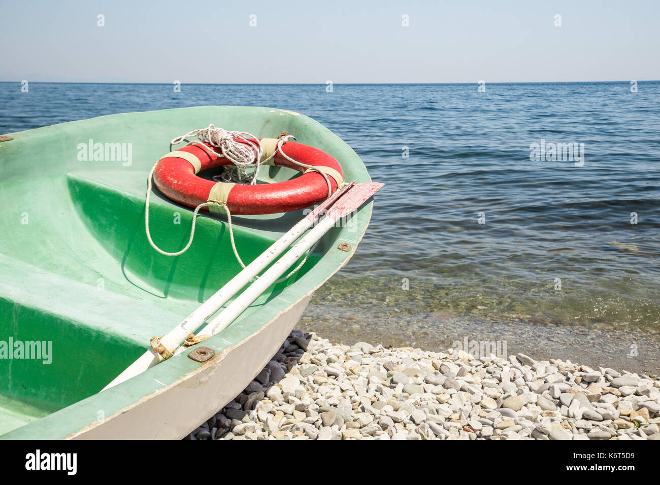 Old green paddle lifeboat on a pebble beach. There is paddles and red ...