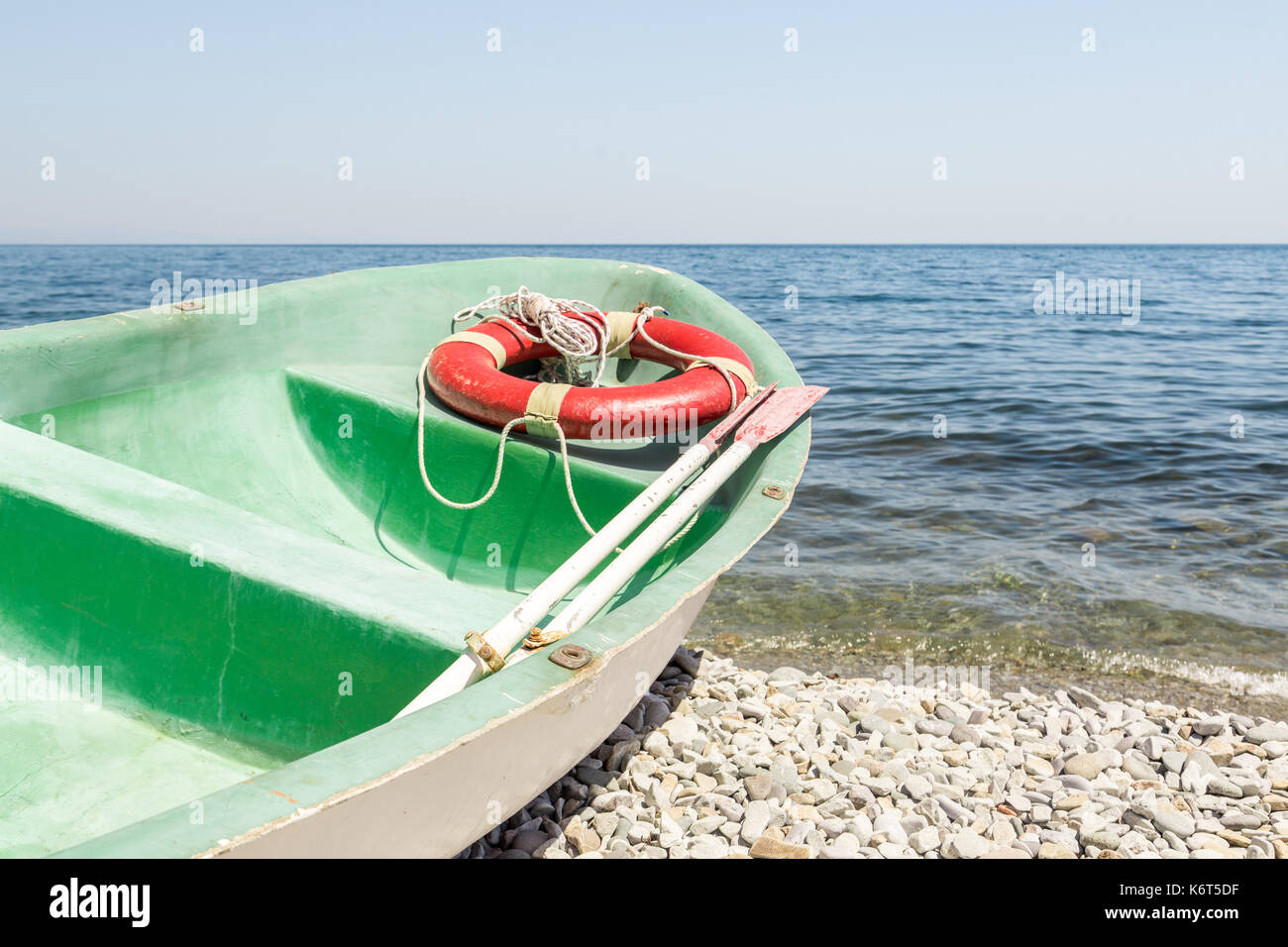 Old green paddle lifeboat on a pebble beach. There is paddles and red ...