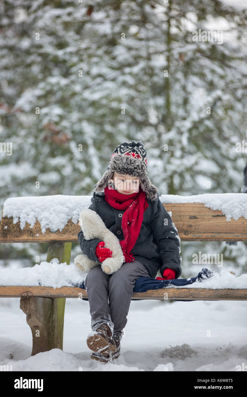 Two children, boy brothers, sitting on a bench in park, wintertime ...