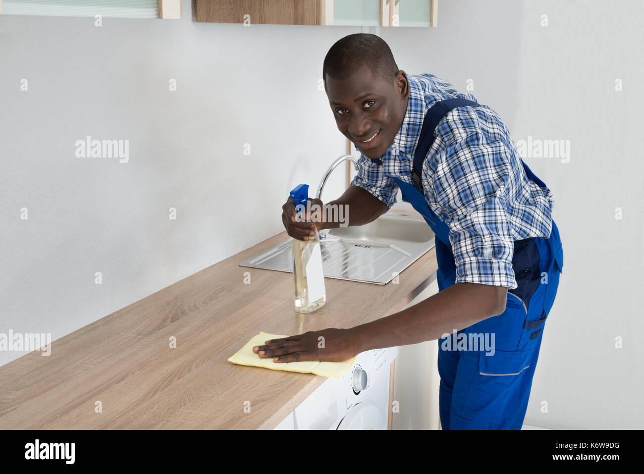 Young Happy Janitor Cleaning Kitchen Worktop With Rag And Cleaning ...