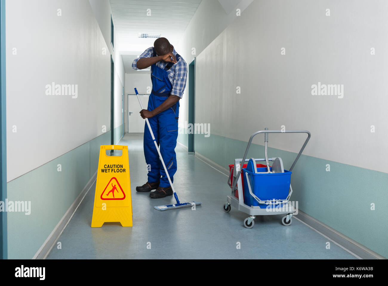 Tired Male Janitor With Cleaning Equipment And Wet Floor Sign In ...