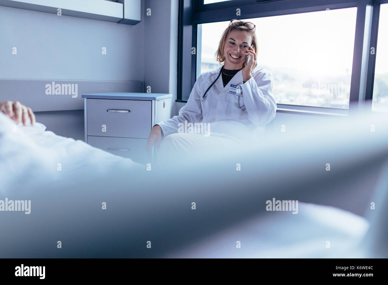 Happy female doctor sitting in hospital room and making a phone call ...