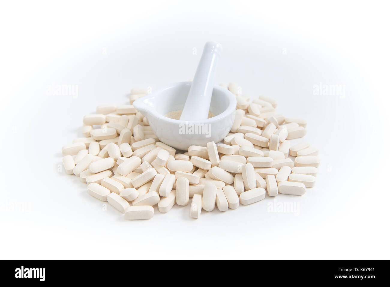 Circular pile of off-white tablets with a mortar and pestle on white ...