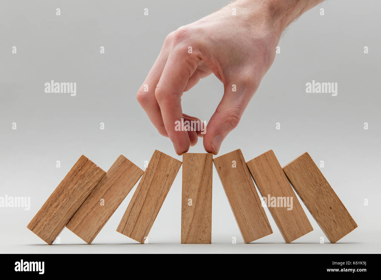 Male hand stopping wooden blocks falling over Stock Photo - Alamy