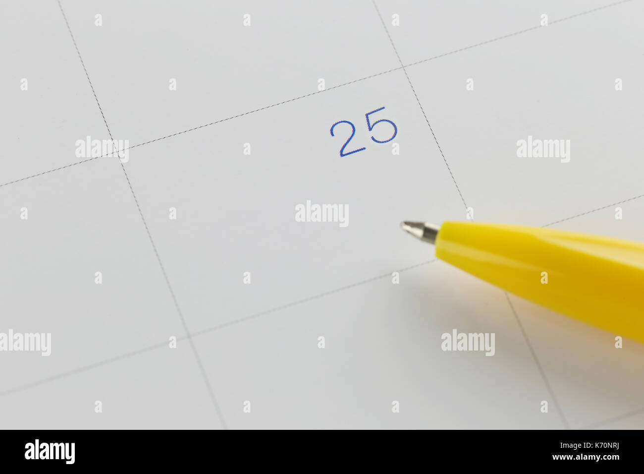 yellow pen points to the number 25 on calendar background in concept of ...
