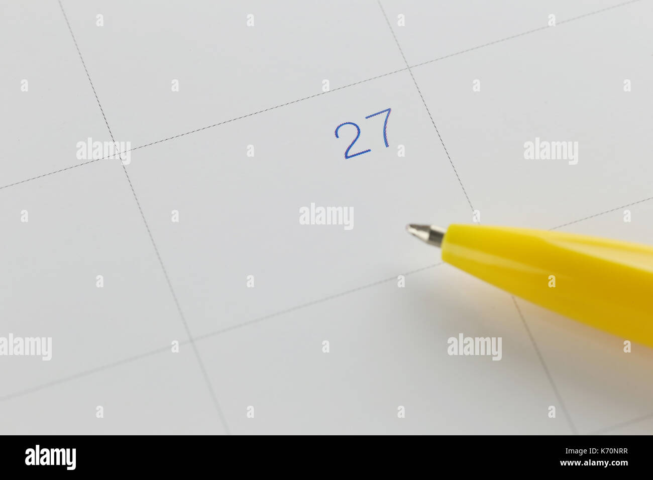 yellow pen points to the number 27 on calendar background in concept of ...