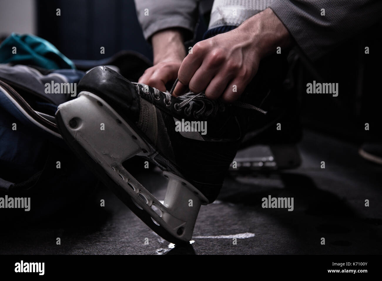 Low section of male ice hockey player tying skate in dressing room ...