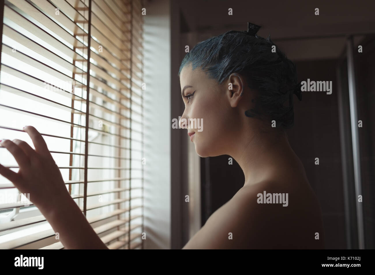 Side view of thoughtful young woman looking through window at home ...
