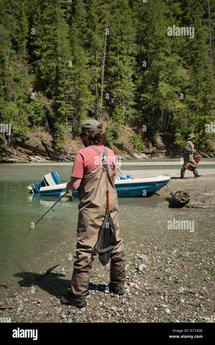 Rear view of fishing in river while standing at riverbank during sunny ...