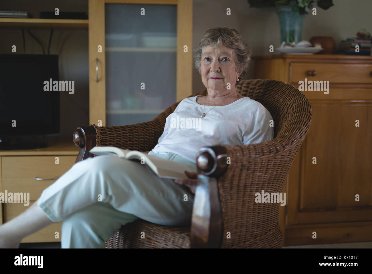 Portrait of senior woman sitting on chair with book in living room ...
