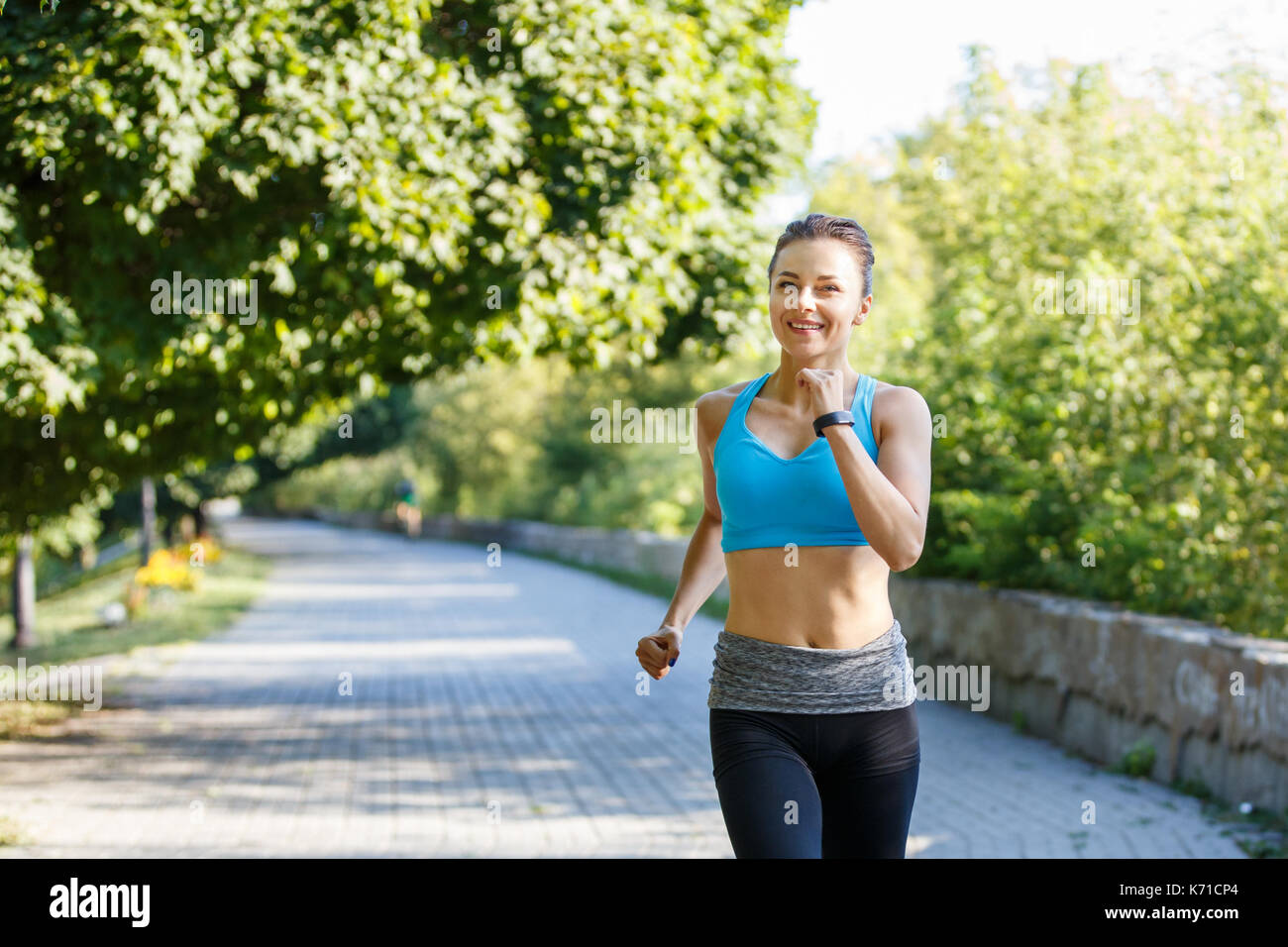 Beautiful young woman in blue top jogging in park. Healthy girl ...