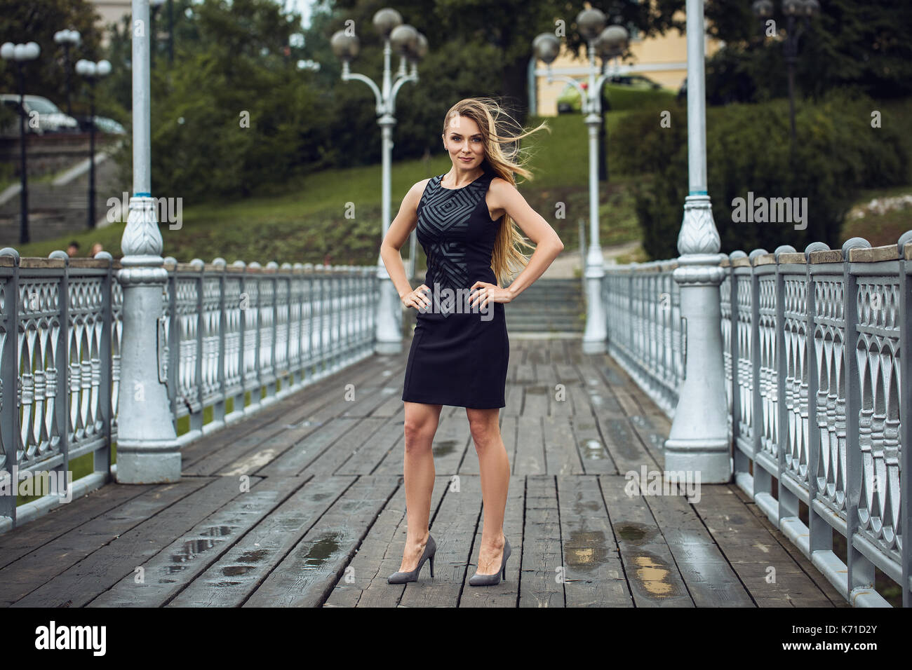 Outdoor lifestyle portrait of blonde young woman in stylish black dress ...