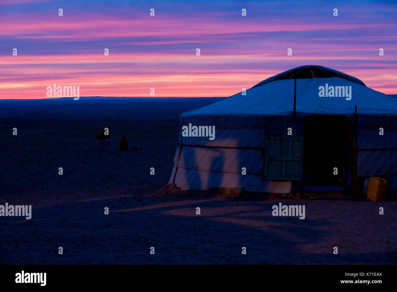 A yurt tent partially illuminated under a colorful purple sunset sky in ...