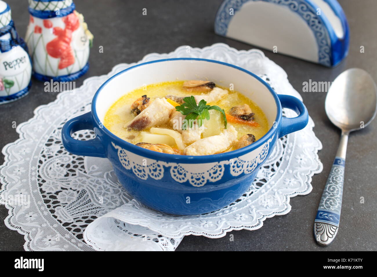 Creamy soup with fish fillet and mussels in a blue ceramic pot on a ...