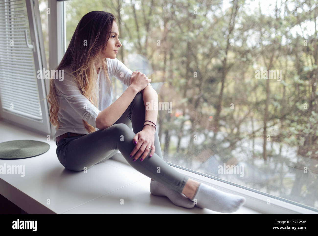 Melancholic woman sitting on window ledge at home Stock Photo - Alamy